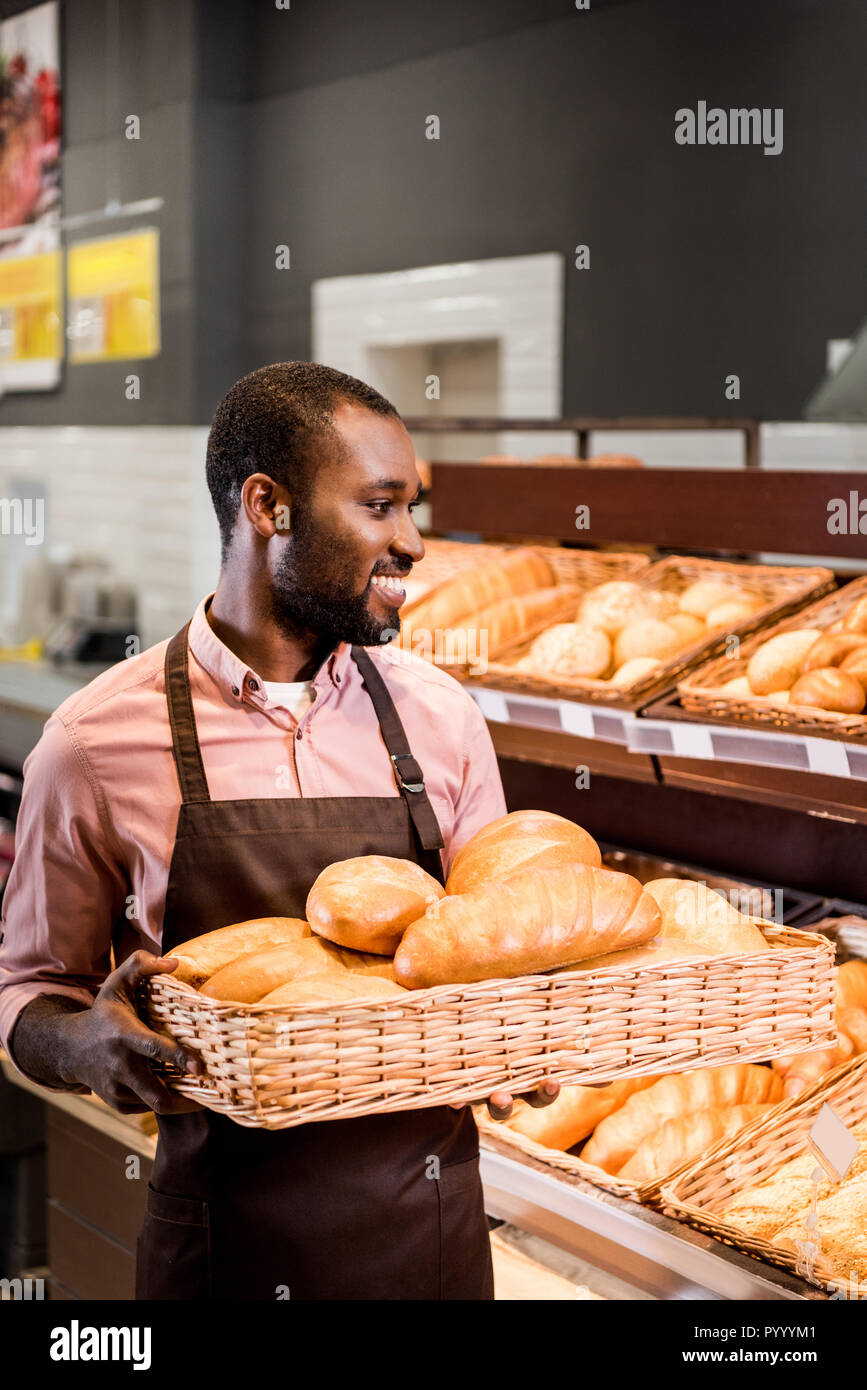 african american male shop assistant in apron holding loaves of bread ...