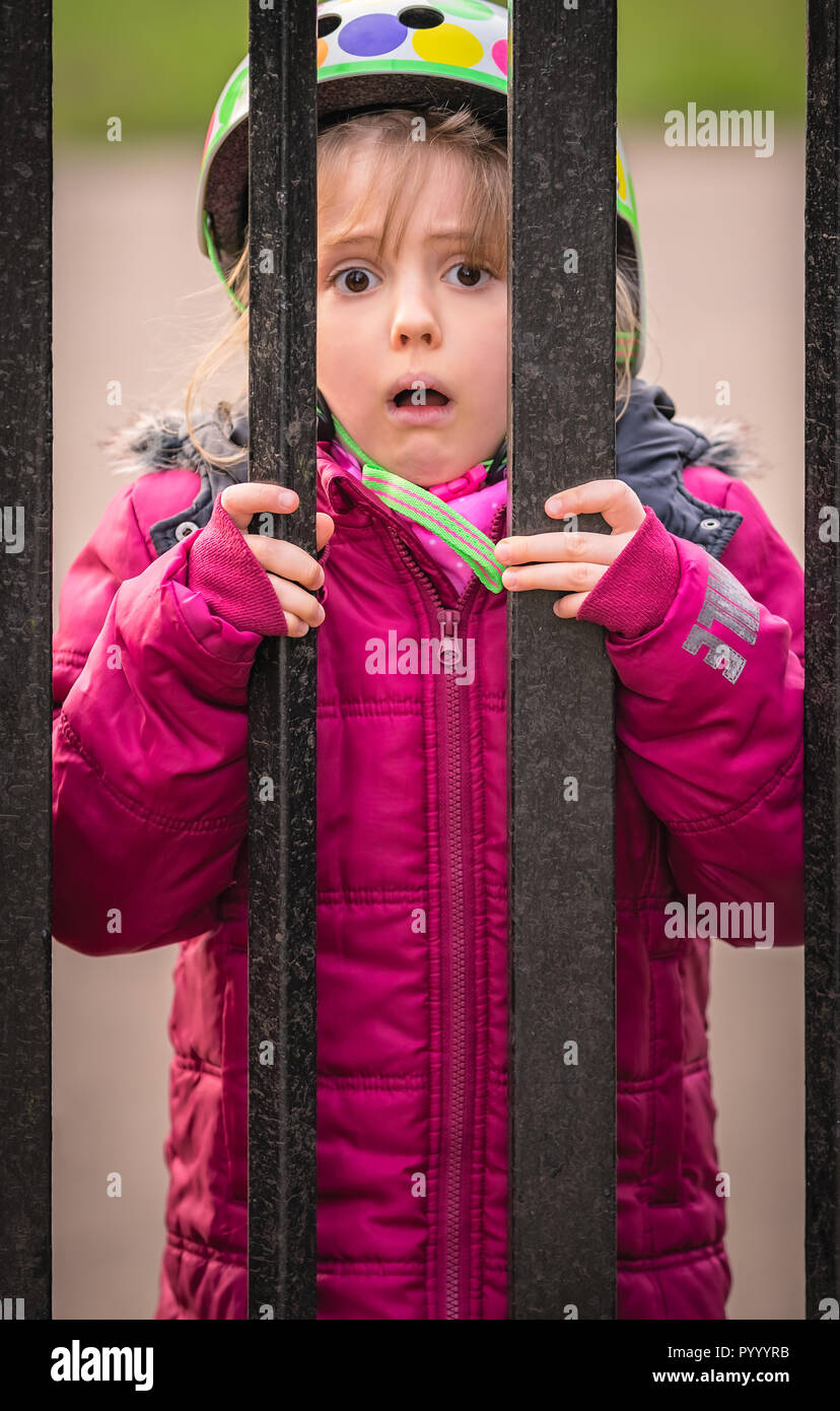 Little cute Caucasian girl dressed in pink jacket standing behind metal ...