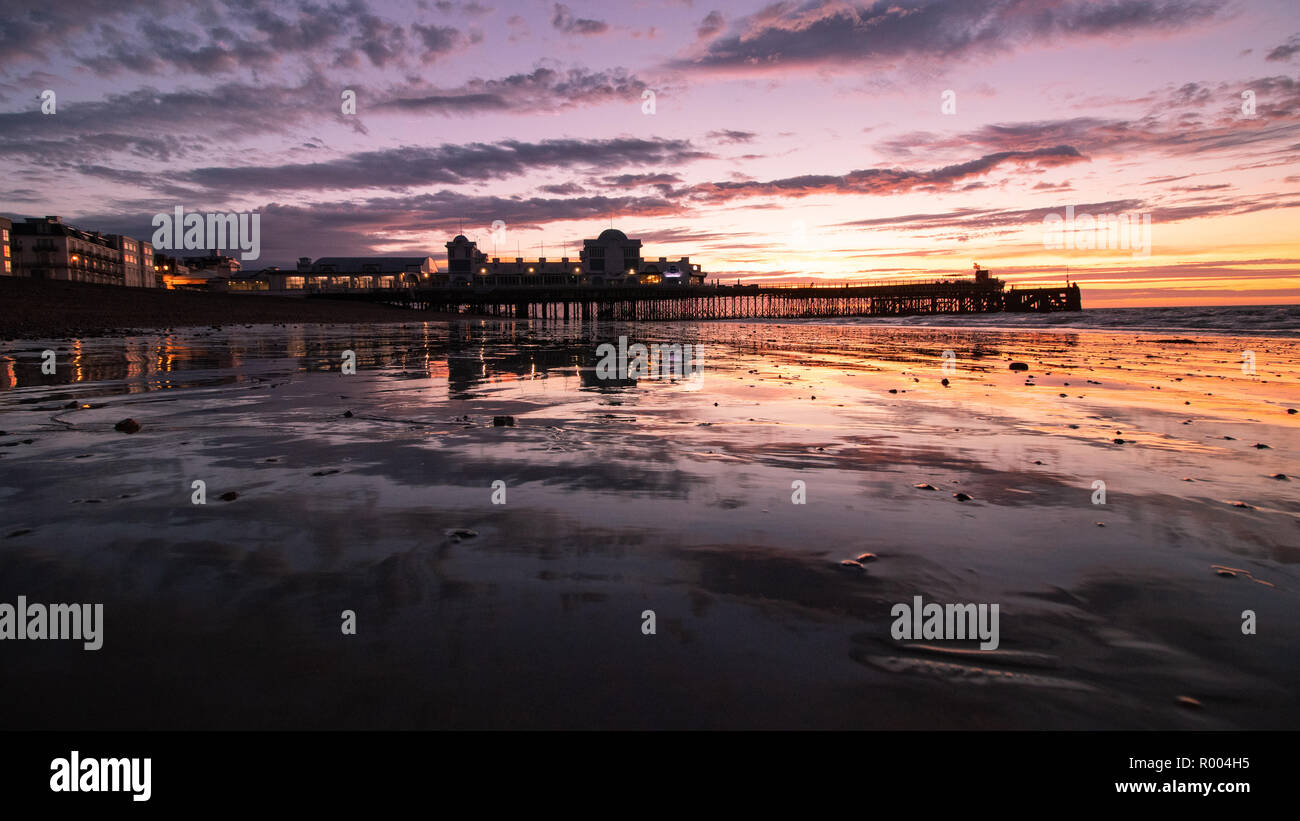 an old British victorian pier reflecting in the wet sands at sunrise ...