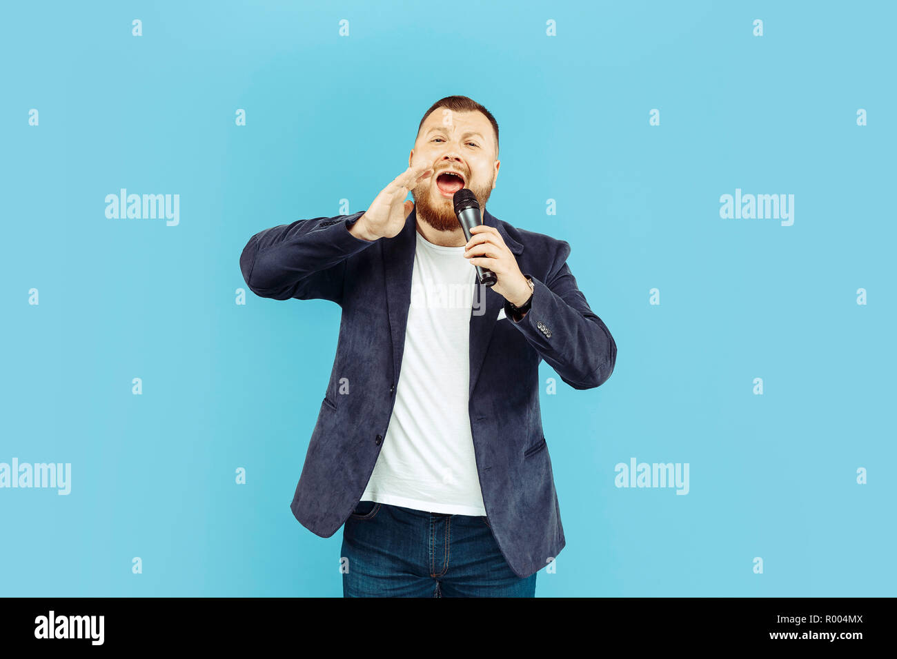 Young man with microphone on blue studio background, leading concept ...