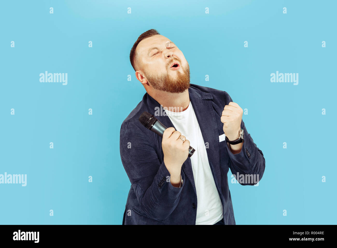 Young man with microphone on blue studio background, leading concept ...