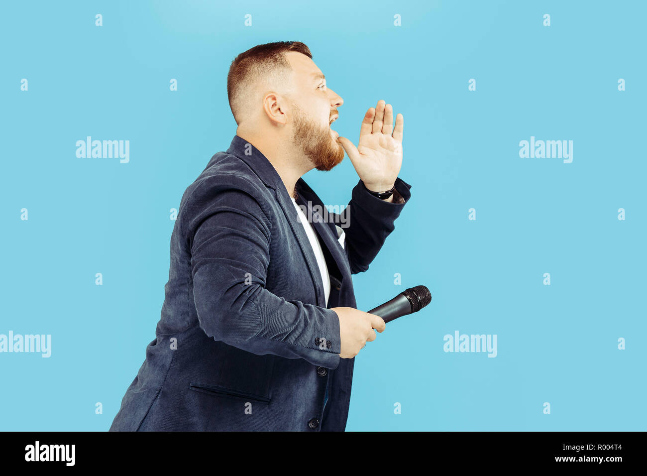 Young man with microphone on blue studio background, leading concept ...