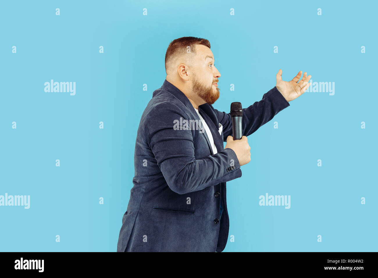 Young man with microphone on blue studio background, leading concept ...