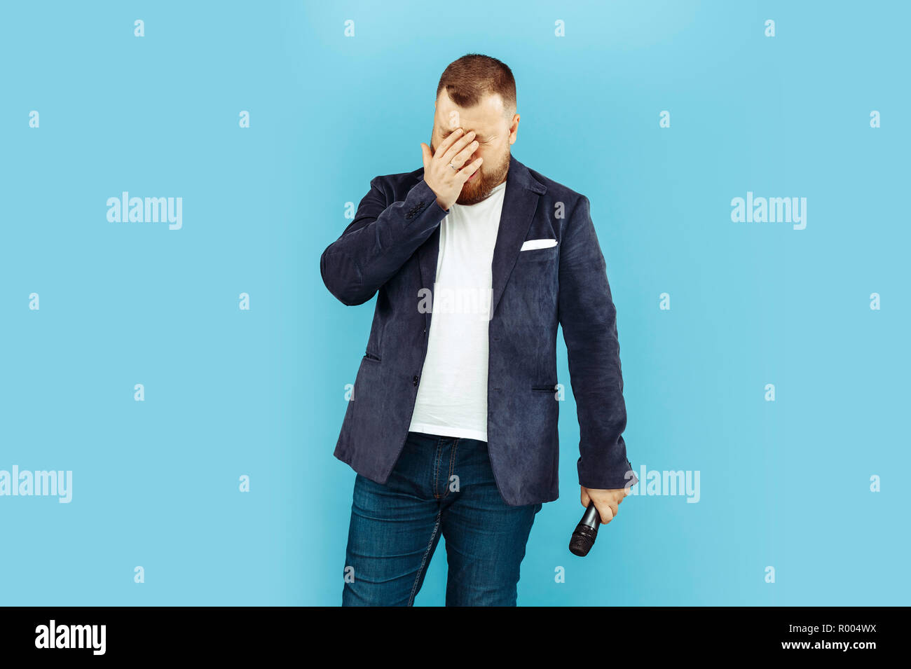 Young man with microphone on blue studio background, leading concept ...