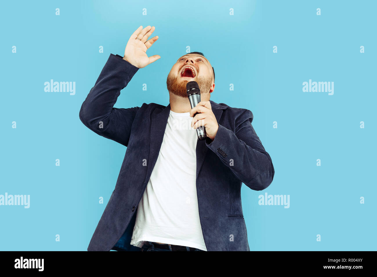 Young man with microphone on blue studio background, leading concept ...