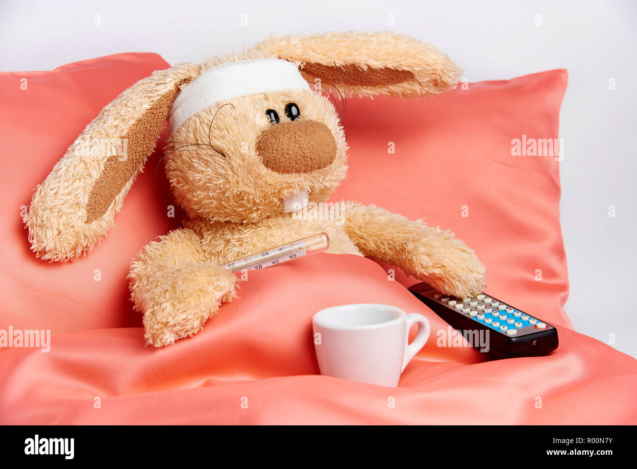 A toy unhealthy rabbit with a thermometer and a TV remote control is ...