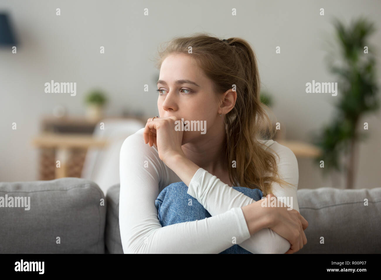 Sad woman sitting on couch alone at home Stock Photo - Alamy