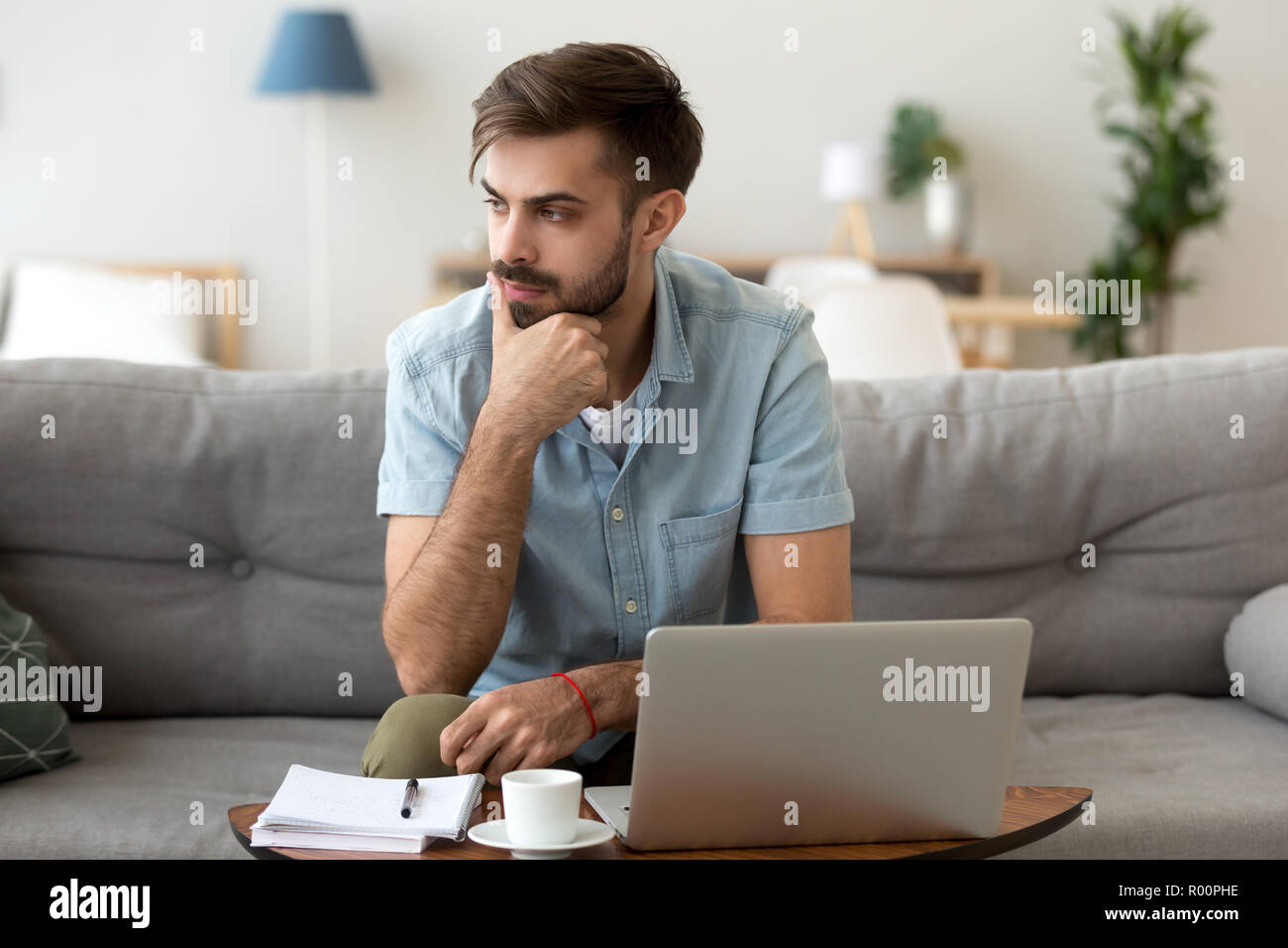 Man sitting on couch thinking at home Stock Photo - Alamy
