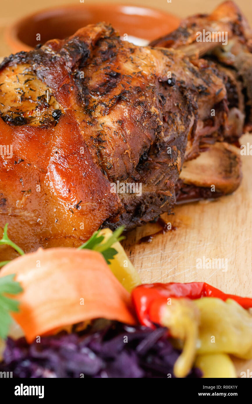Roasted european pork knuckle on wood platter with vegetable garnish ...