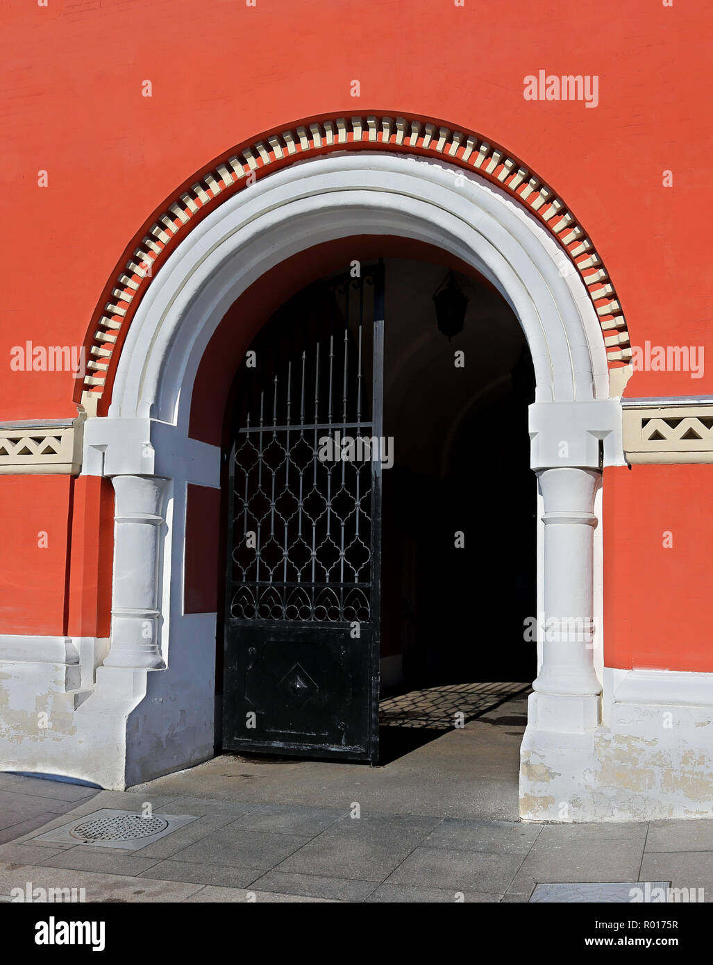 Aged buildings red brick wall with entrance arch and a black metal gate ...