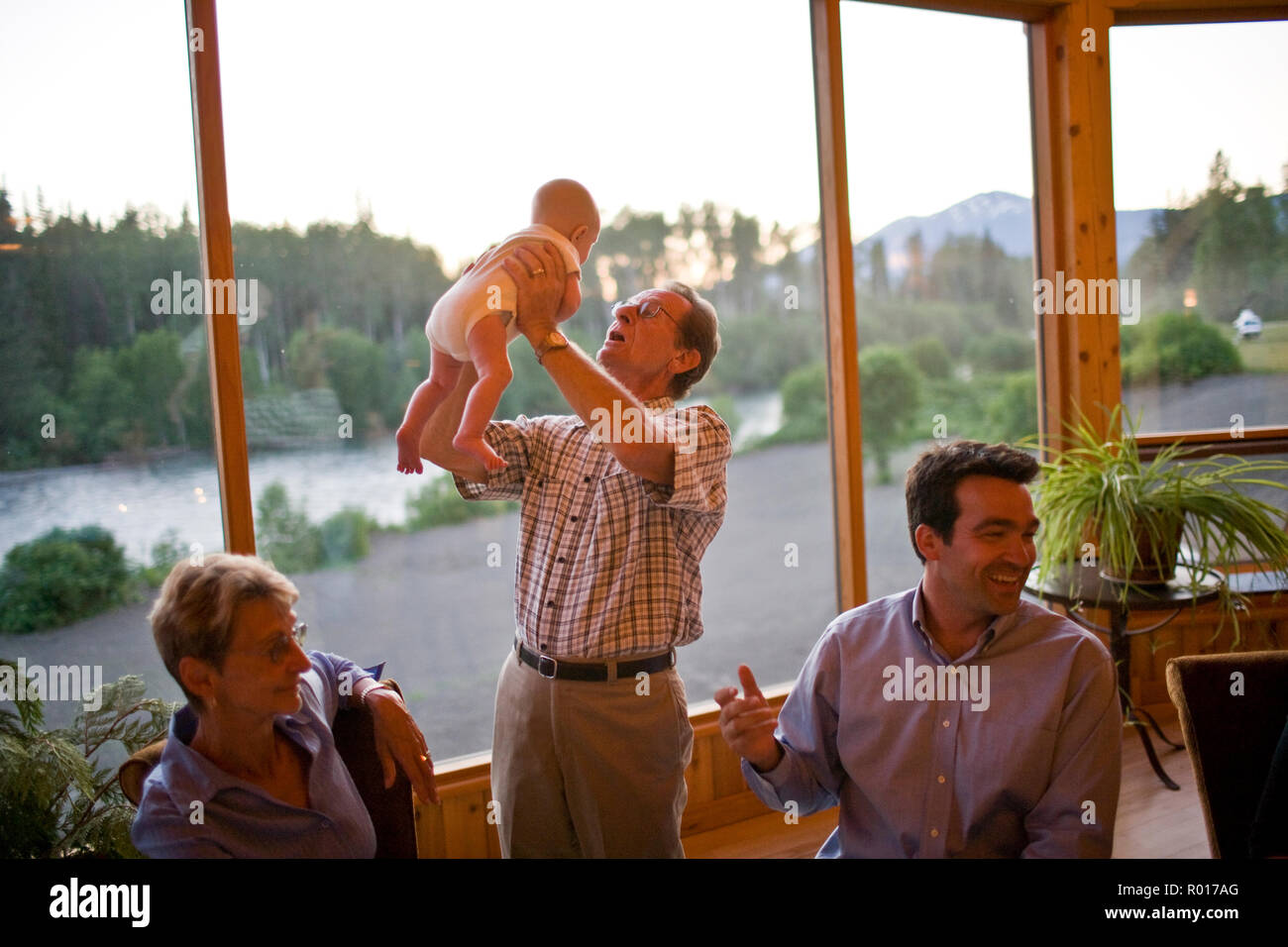 Grandfather holding up baby behind seated family members Stock Photo ...