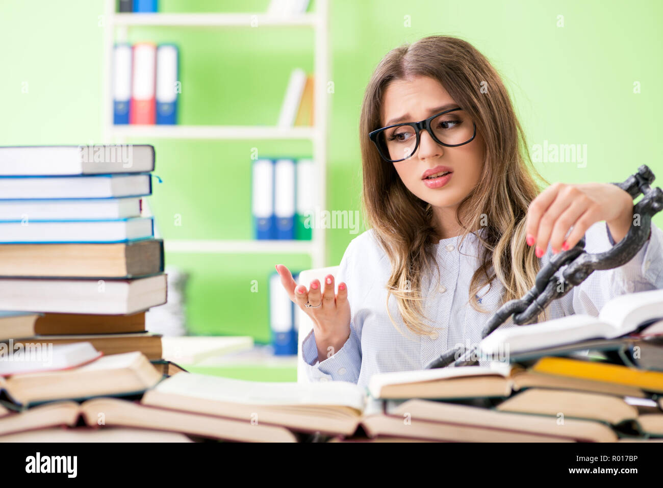 Young female student chained to the desk and preparing for exams with ...
