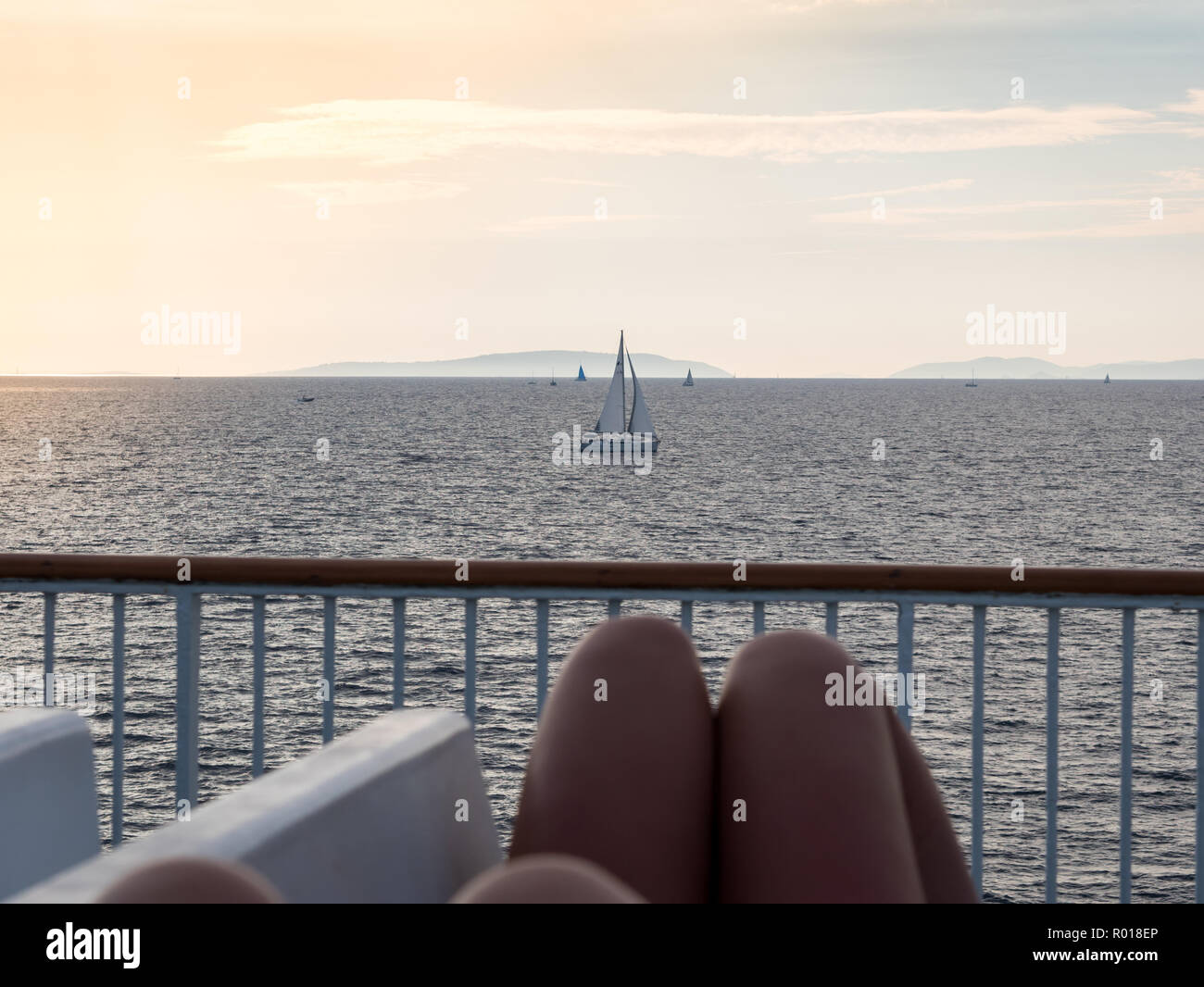Woman legs on cruise ship with sailboats at background on calm blue sea ...