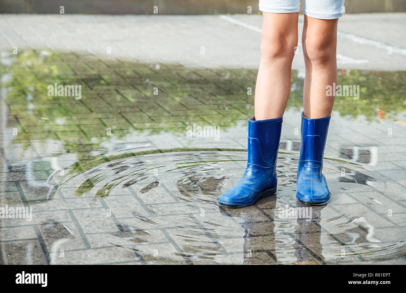 girl in rubber boots standing in a puddle after a rain outdoor on ...