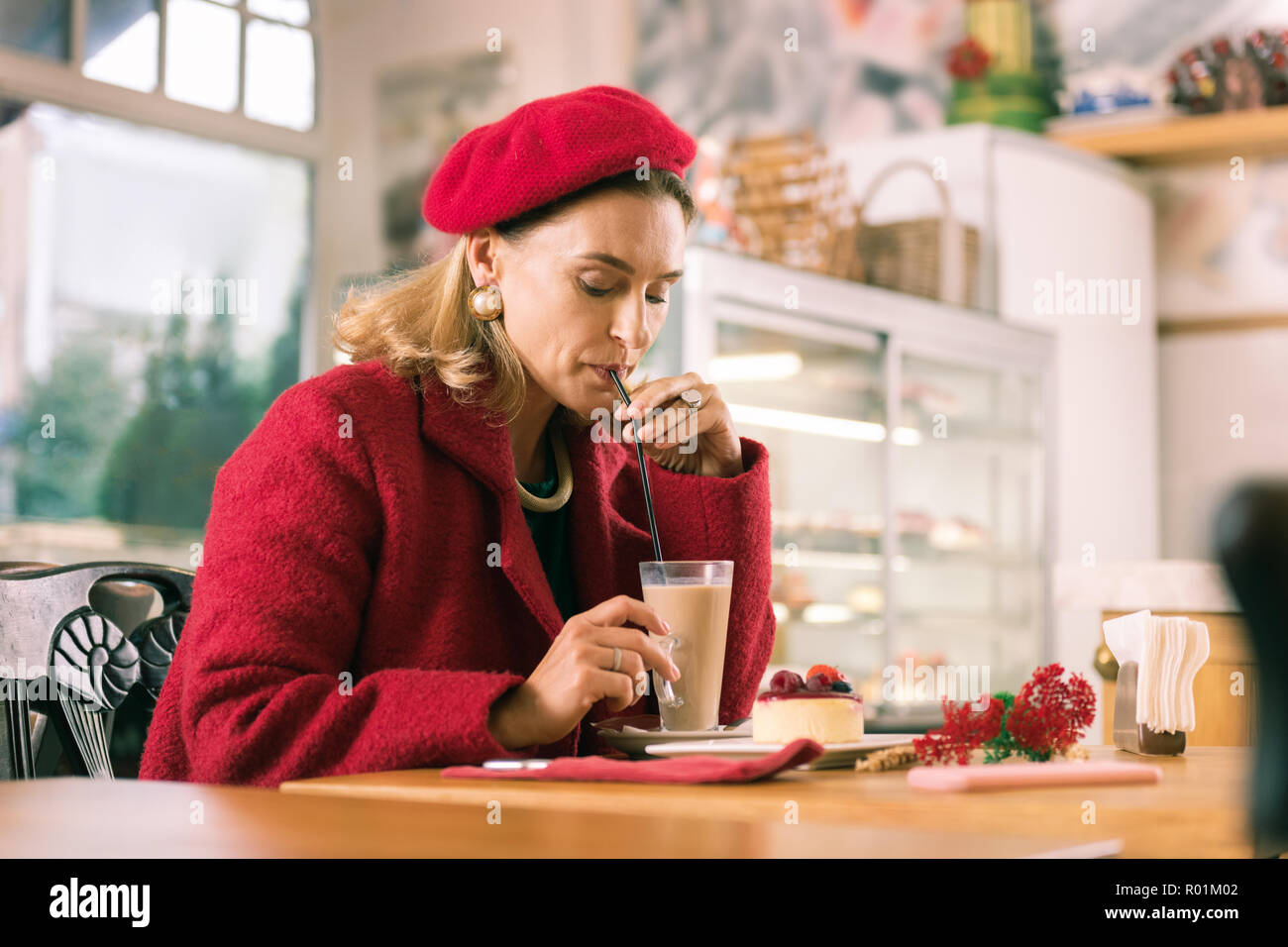 French woman wearing red outfit drinking latte sitting in nice bakery ...