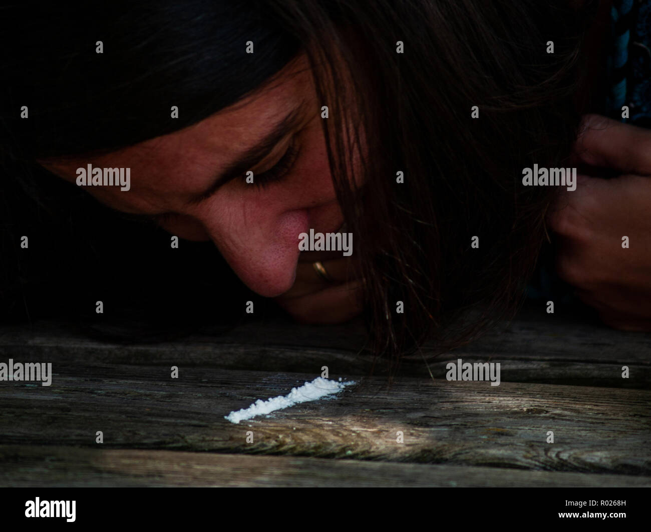 A woman snorting a line of cocaine on a wooden table with a glass of ...