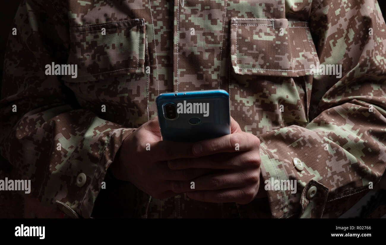 US Army. Young soldier holding a mobile phone standing on dark ...