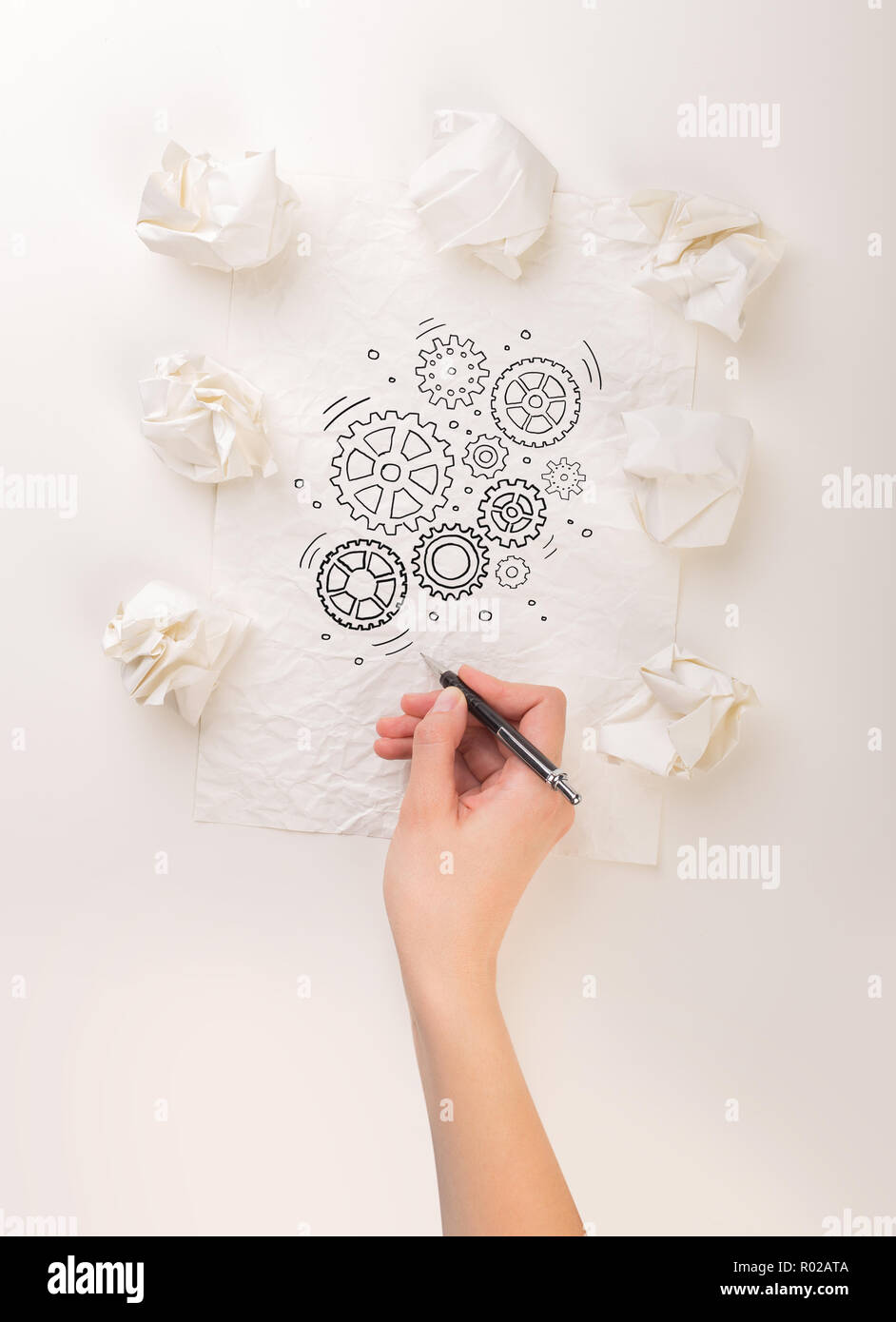 Female hand next to a few crumpled paper balls drawing rotating gears ...