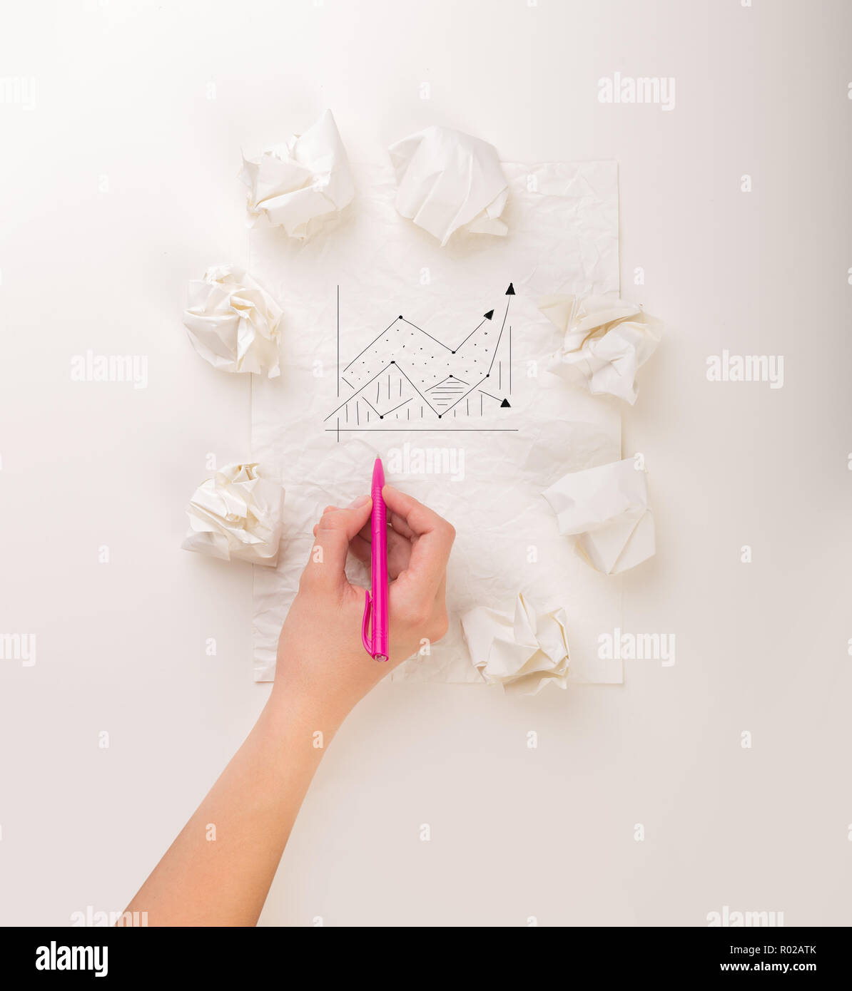 Female hand next to a few crumpled paper balls drawing a progress chart ...