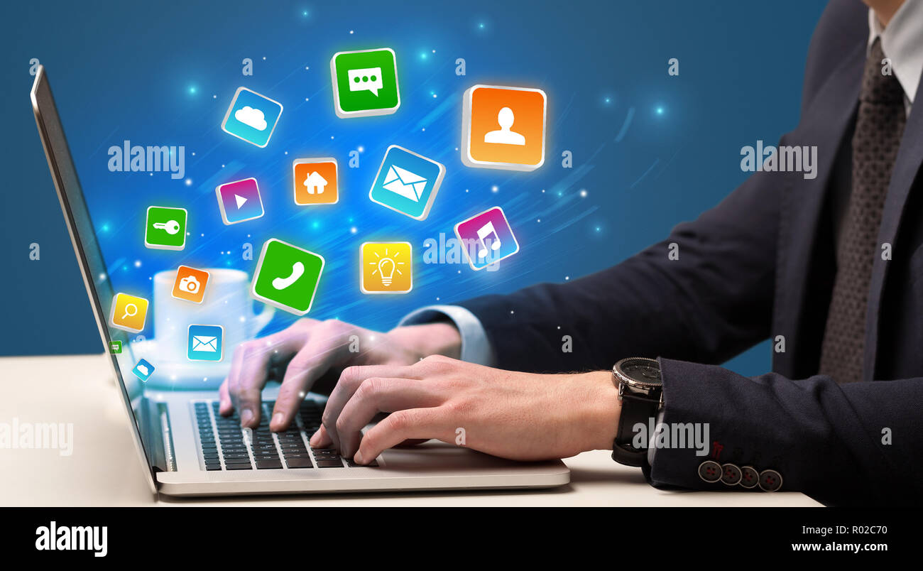 Businessman hand typing on laptop with flying application icons around ...
