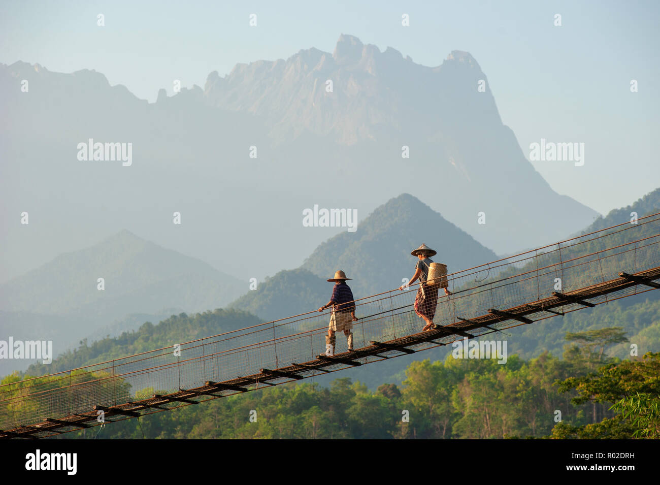 villagers passing through a hanging bridge with Mount Kinabalu at ...