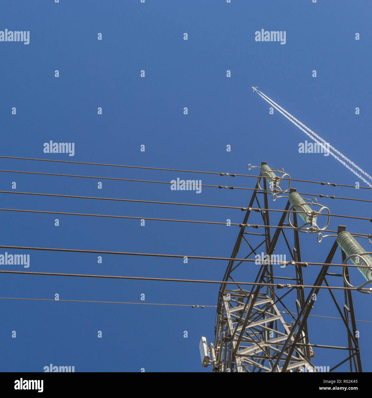 UK electricity pylon with plane and vapour trail overhead. Showing ...