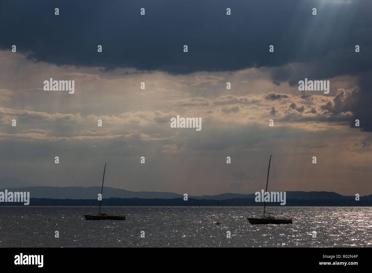 A couple of empty, little sailboat on a lake, beneath a moody sky with ...
