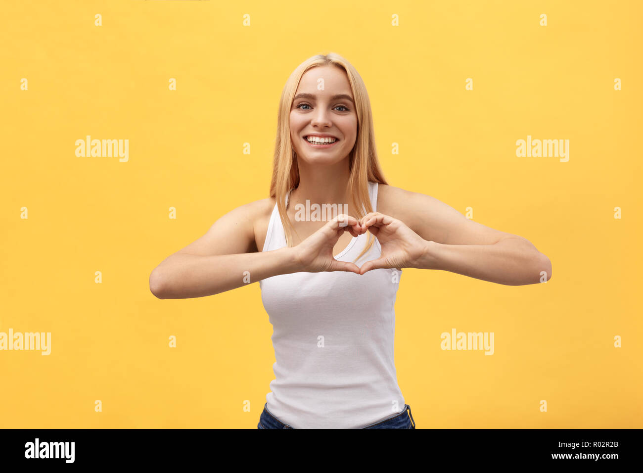 Beautiful Woman Making Heart Shape Sign against a yellow background ...