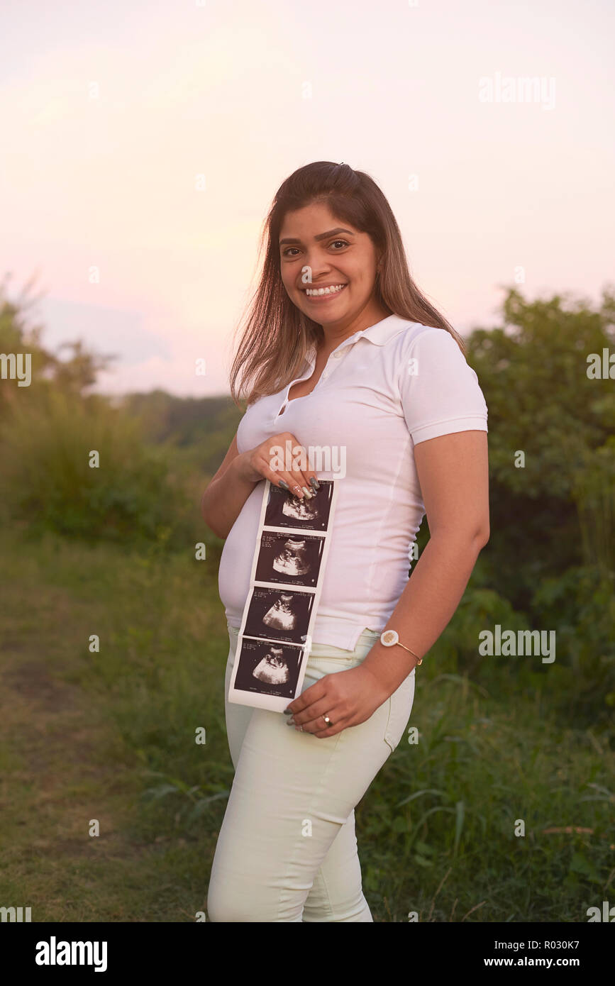 Hispanic pregnant woman with ultrasound print on outdoor background ...