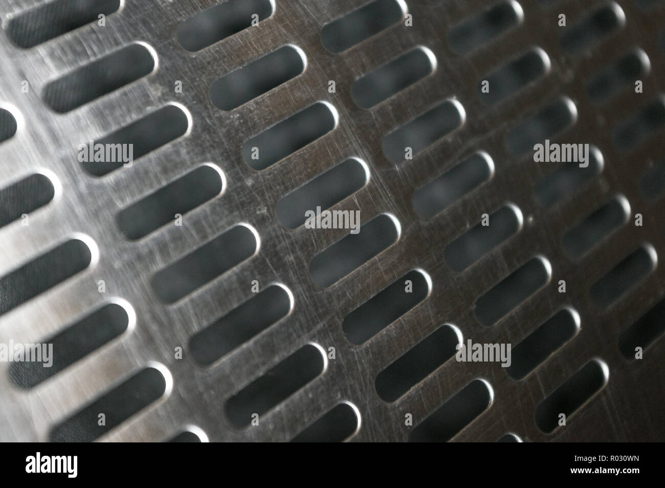 stainless steel grating with oblong holes on black background, close-up ...