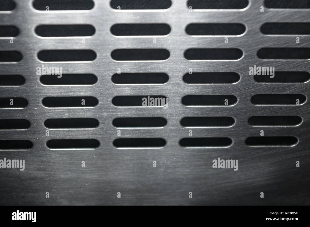 stainless steel grating with oblong holes on black background, close-up ...