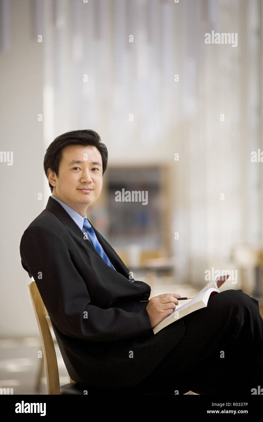 Portrait of a mid-adult teacher reading in a study hall of a school ...