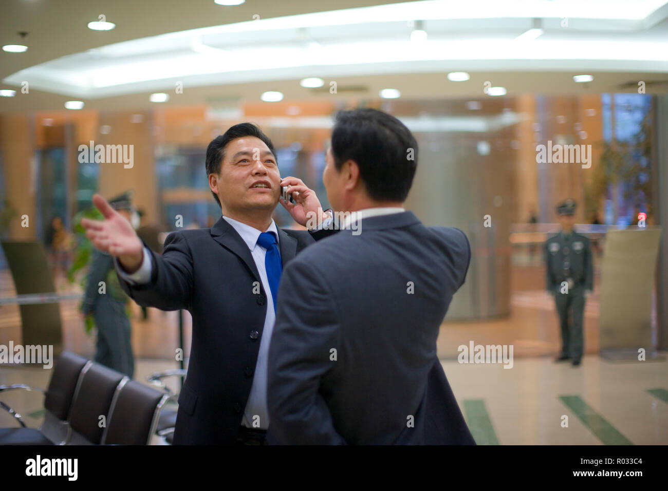 Two businessmen standing opposite each other while talking on their cell phones Stock Photo - Alamy