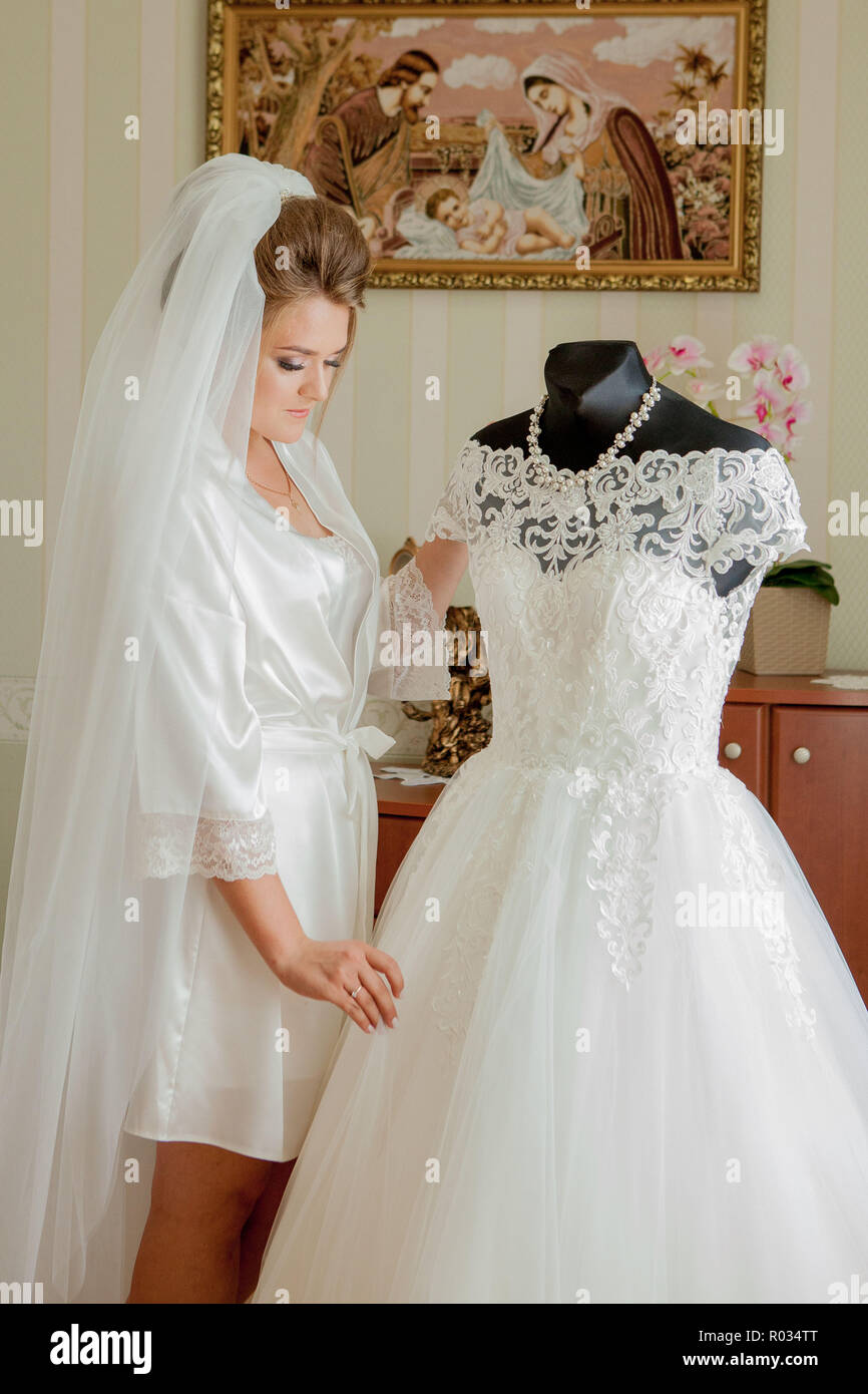The charming bride with bridesmaids stands near wedding dress. Bridal ...