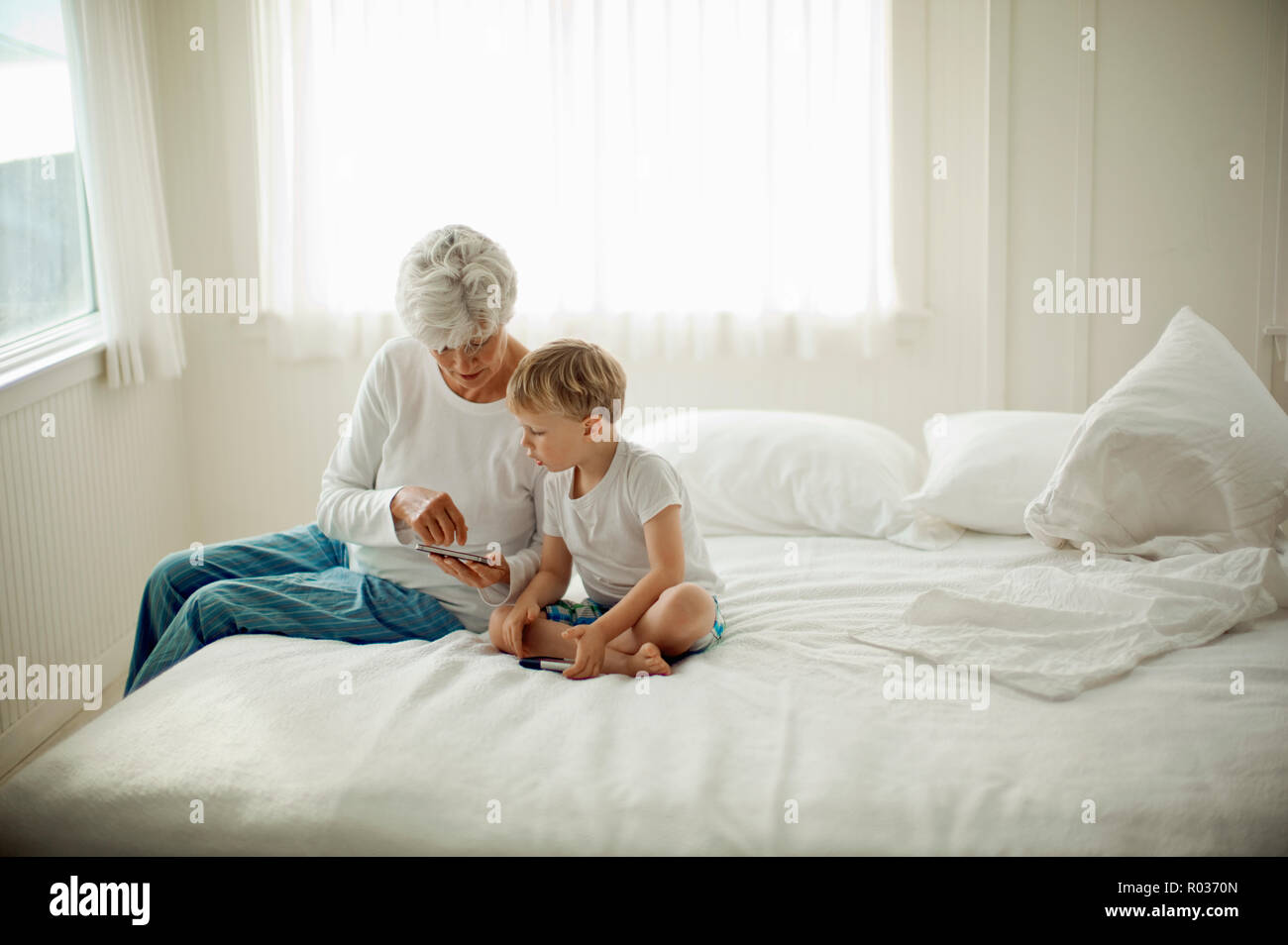 Mature woman in her pajamas sits on a bed with her young grandson and ...
