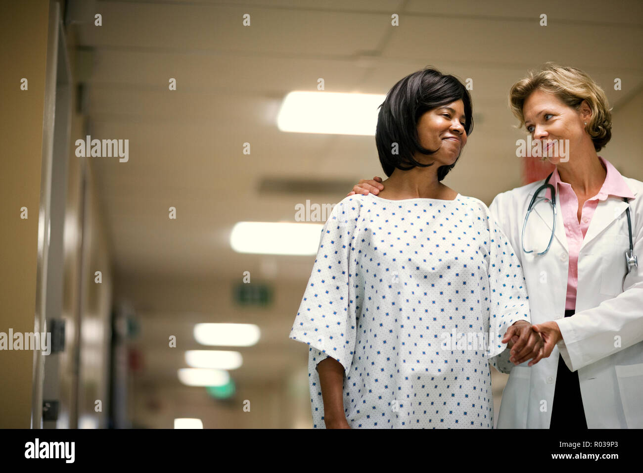 Doctor helping her patient to walk down the corridor for the first time ...