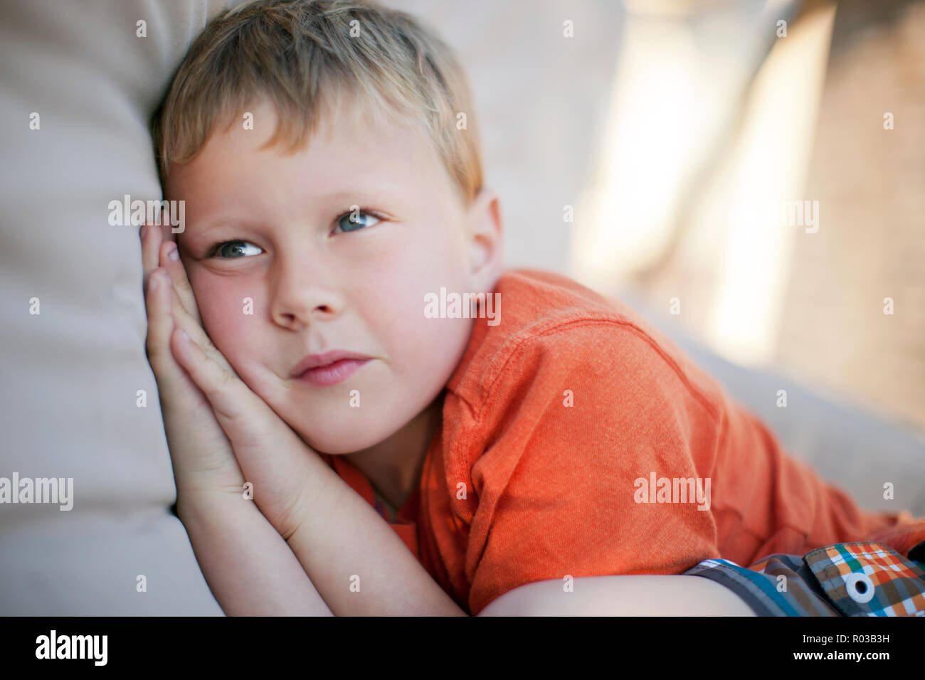 Young boy resting his hands under his head while lying down in bed ...