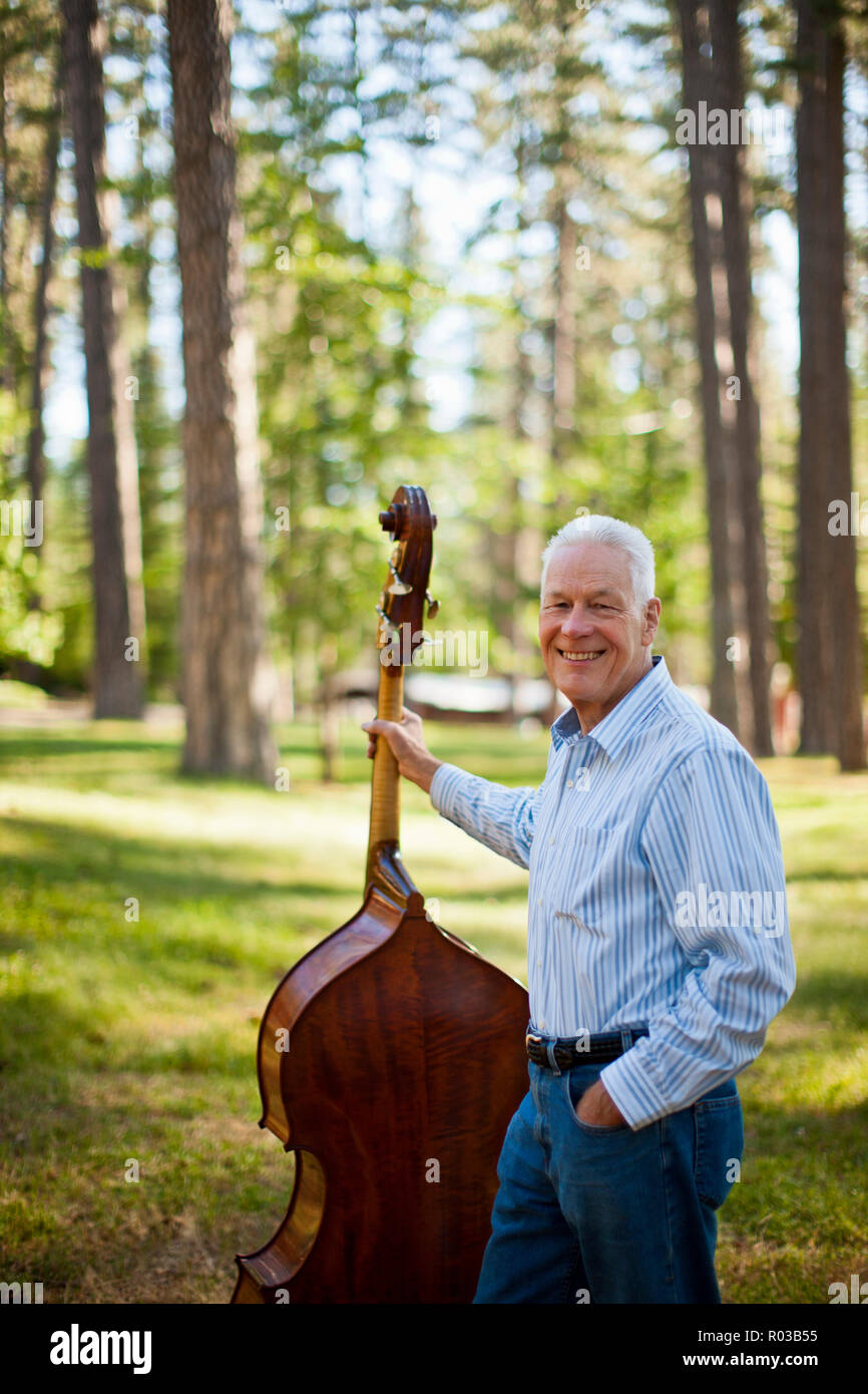 Portrait of a smiling senior man playing a double bass in a forest ...