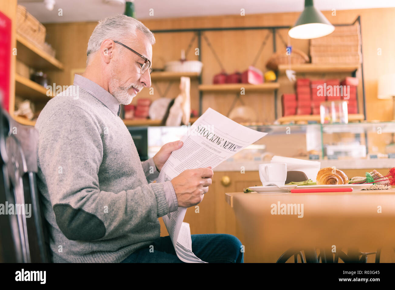 Mature grey-haired man feeling involved in reading local newspaper ...
