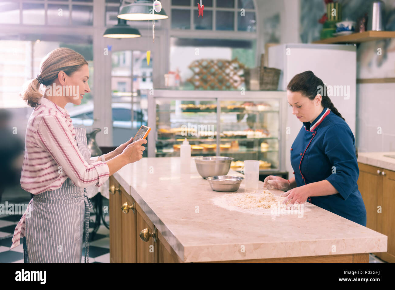 Blonde-haired owner of bakery filming her chef cooking croissants Stock ...