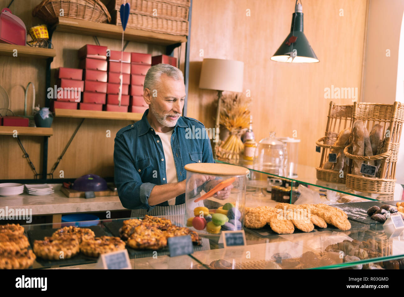 Bearded grey-haired owner of bakery selling cookies in the morning ...