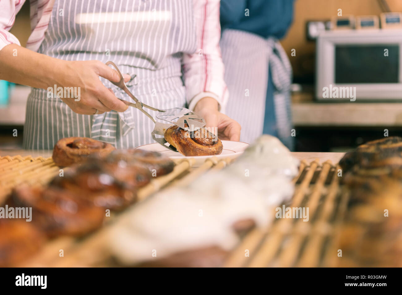 Woman working in bakery putting nice cinnamon bun on plate Stock Photo ...