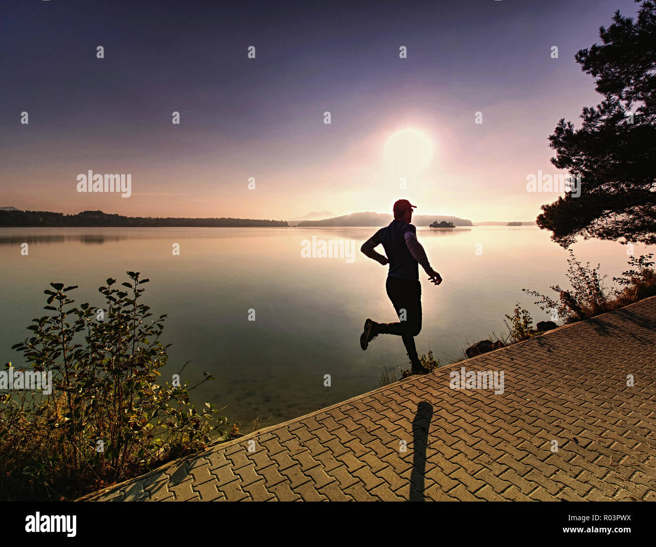 Tall slim man is running along lake in park in sunny daybreak. Misty ...