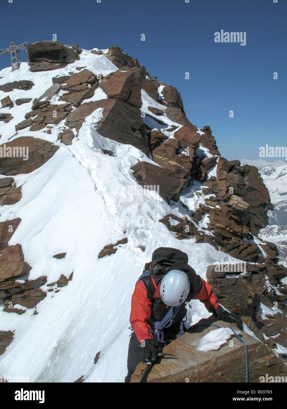 mountain climber on a narrow rock and snow ridge on his way down from a ...