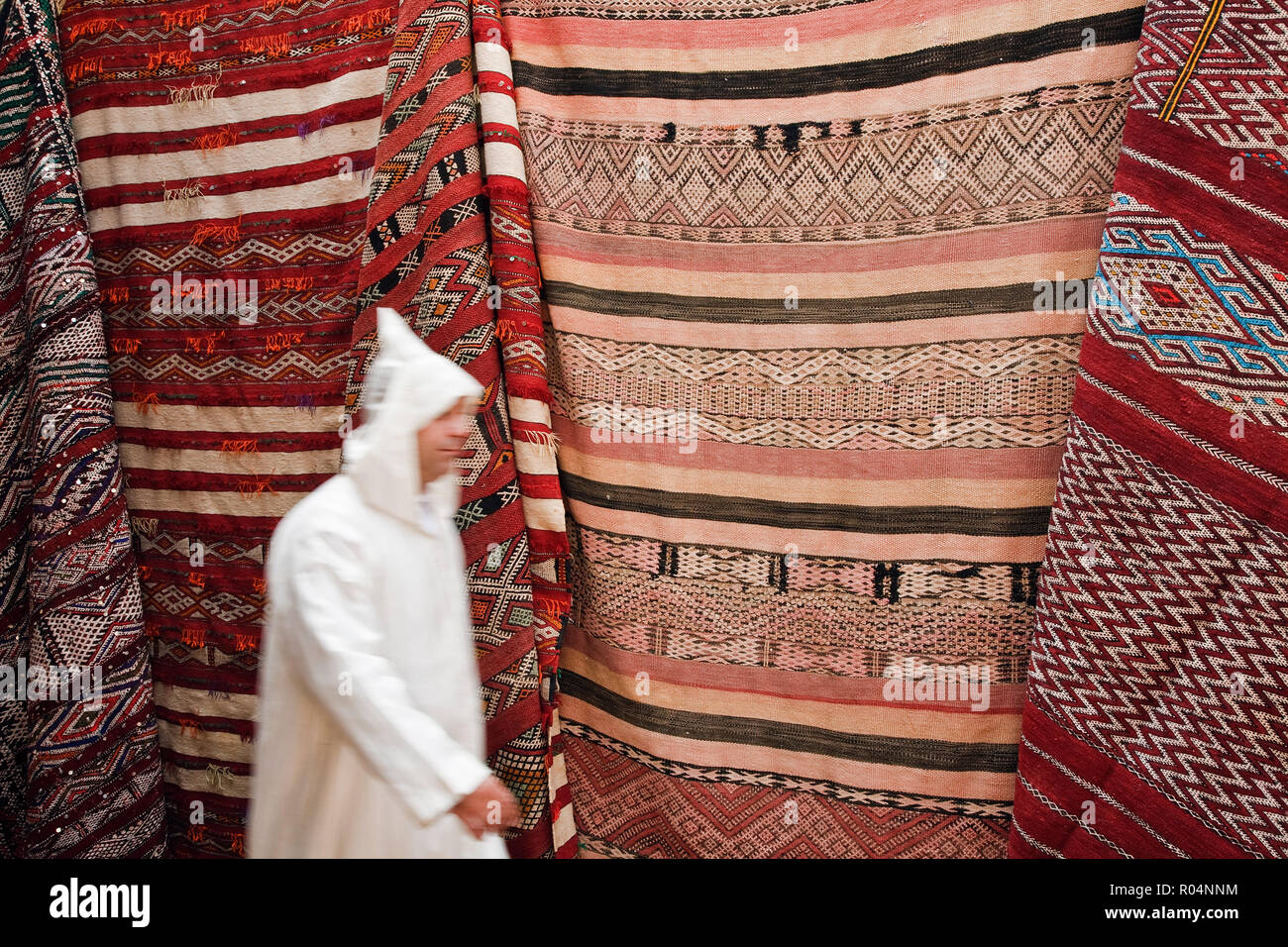 Man in traditional Moroccan clothing walking past colourful fabrics in ...