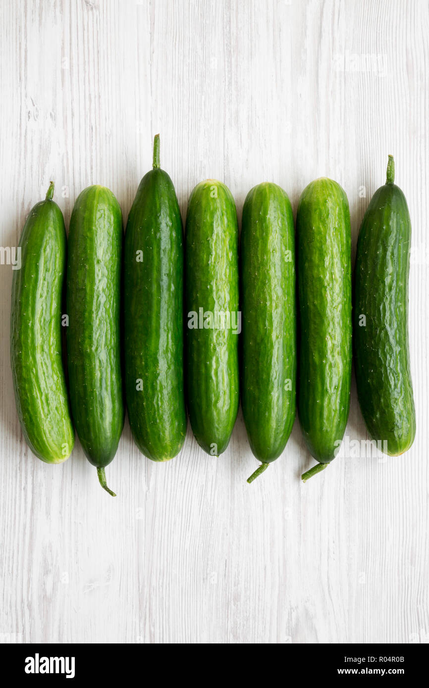 Flat lay of raw organic green cucumbers on white wooden background. Top ...