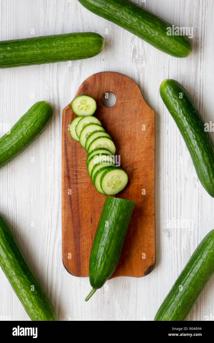 Chopped green cucumbers on wooden board over white wooden background, overhead view. Flat lay ...