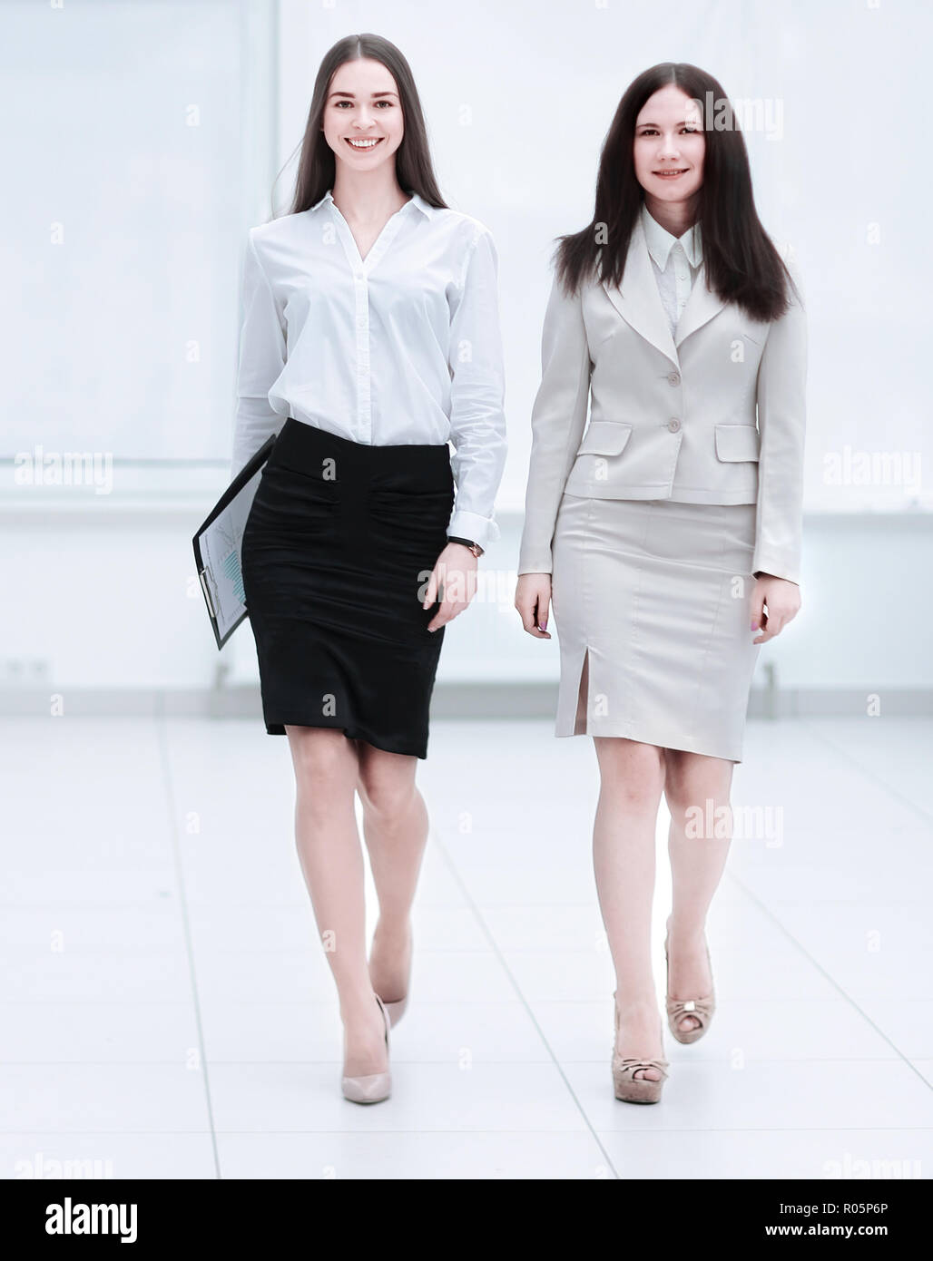 two confident young businesswomen walking down the hall in the office ...