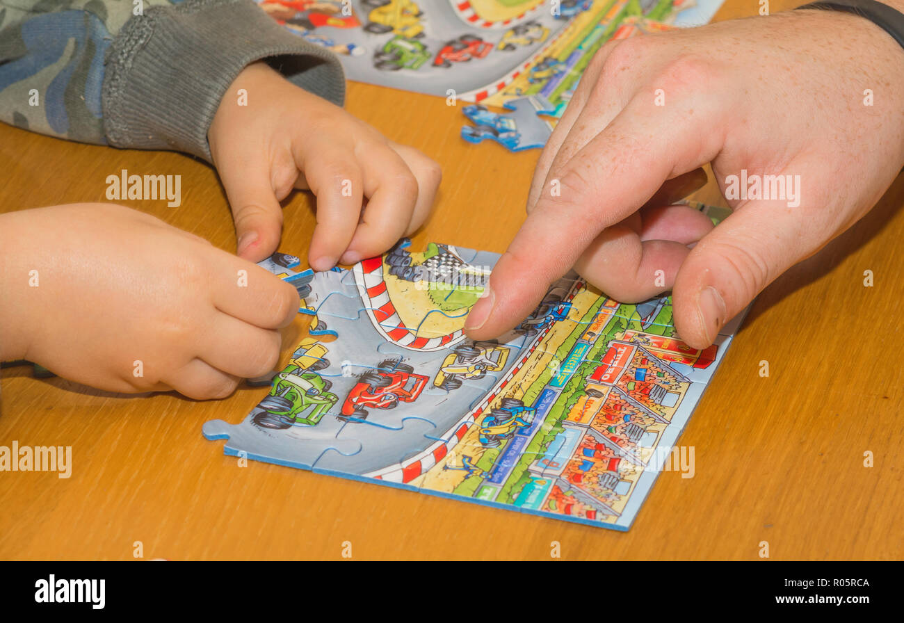 little kid playing with puzzles on wooden table together with parent ...