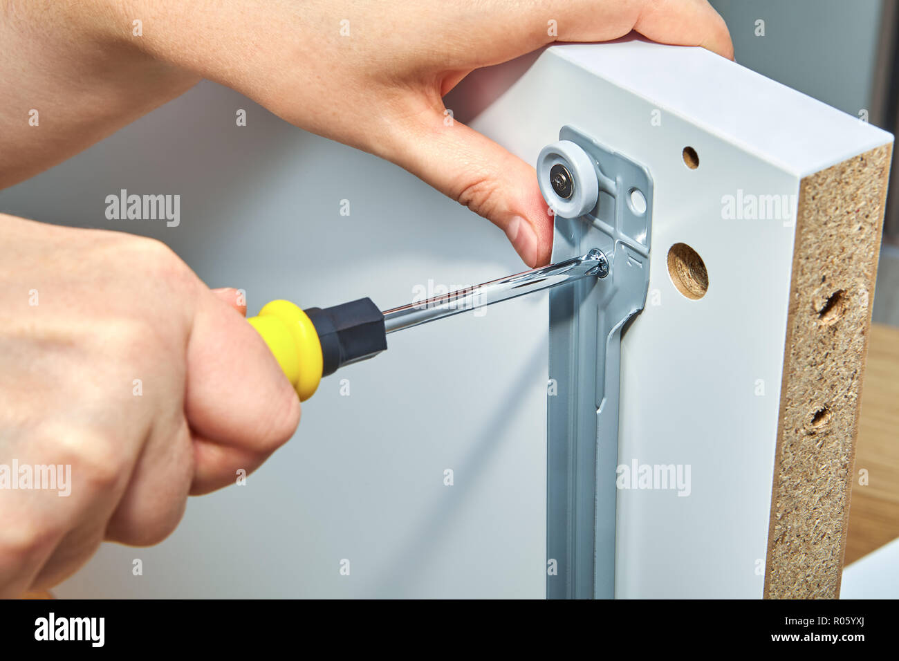The furniture assembler is tightening the screw in the drawer slide ...